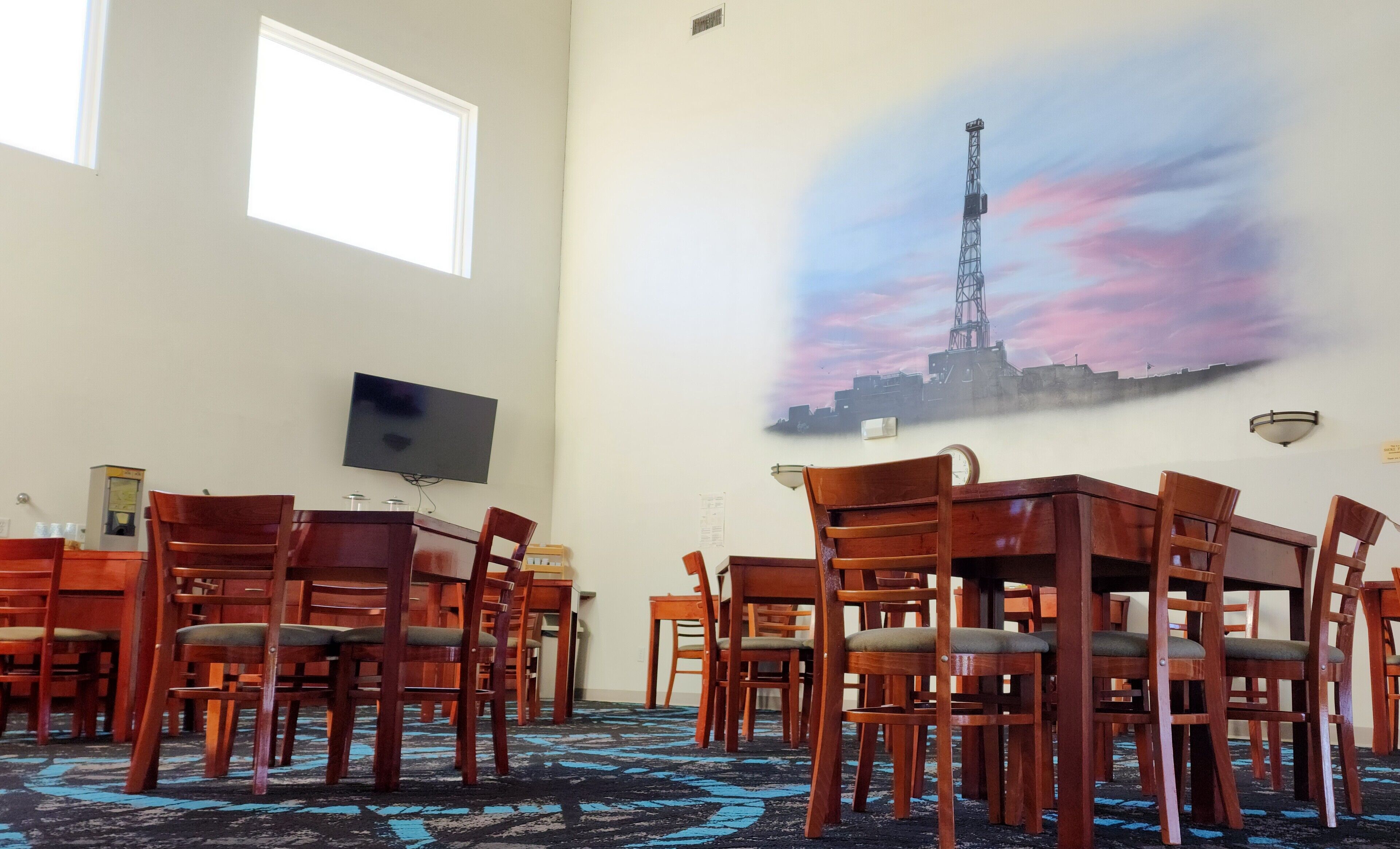 Sala de conferências com uma grande mesa e várias cadeiras, uma TV de tela plana na parede e um mural de uma paisagem urbana com uma torre.