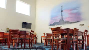 Sala de conferências com uma grande mesa e várias cadeiras, uma TV de tela plana na parede e um mural de uma paisagem urbana com uma torre.