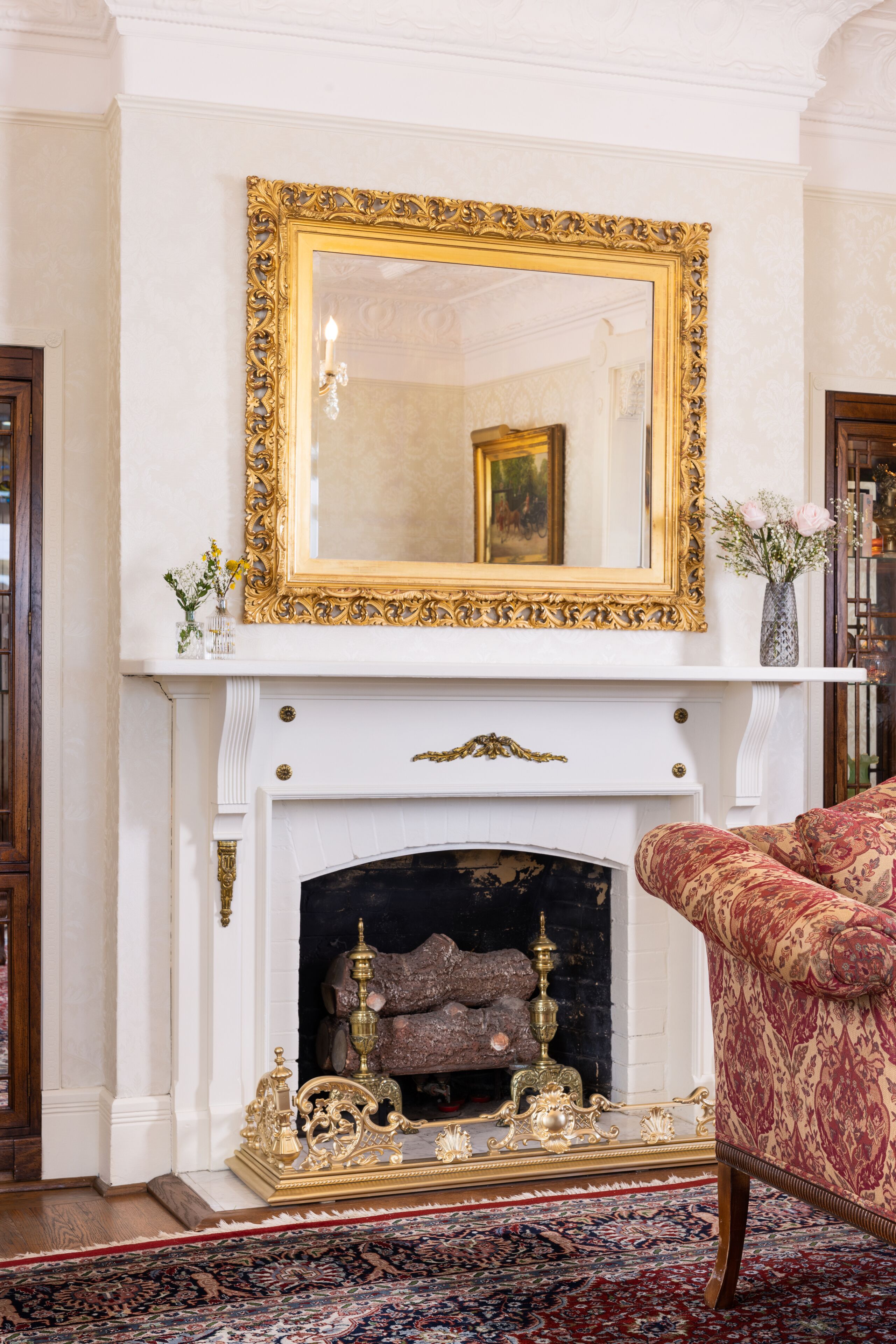 Quarto com lareira, espelho ornamentado e poltrona estampada.