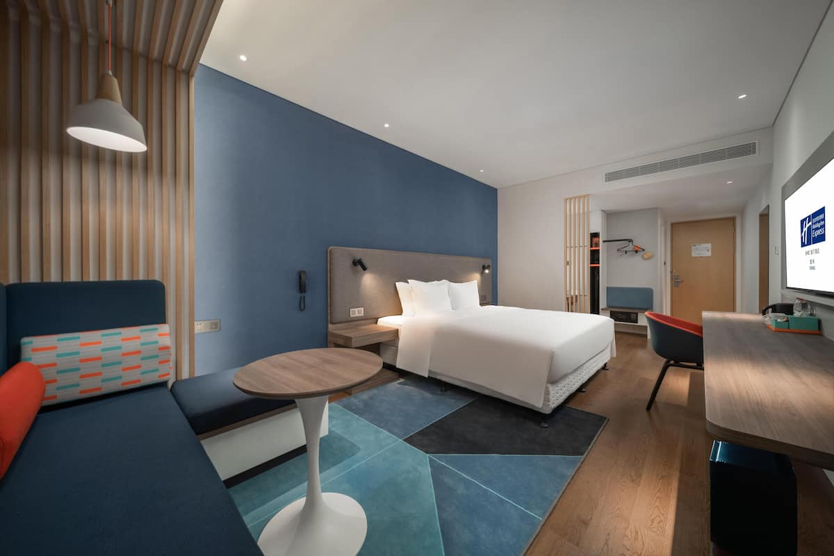 Quarto de hotel moderno com cama, escrivaninha, cadeira, sofá e uma pequena mesa.