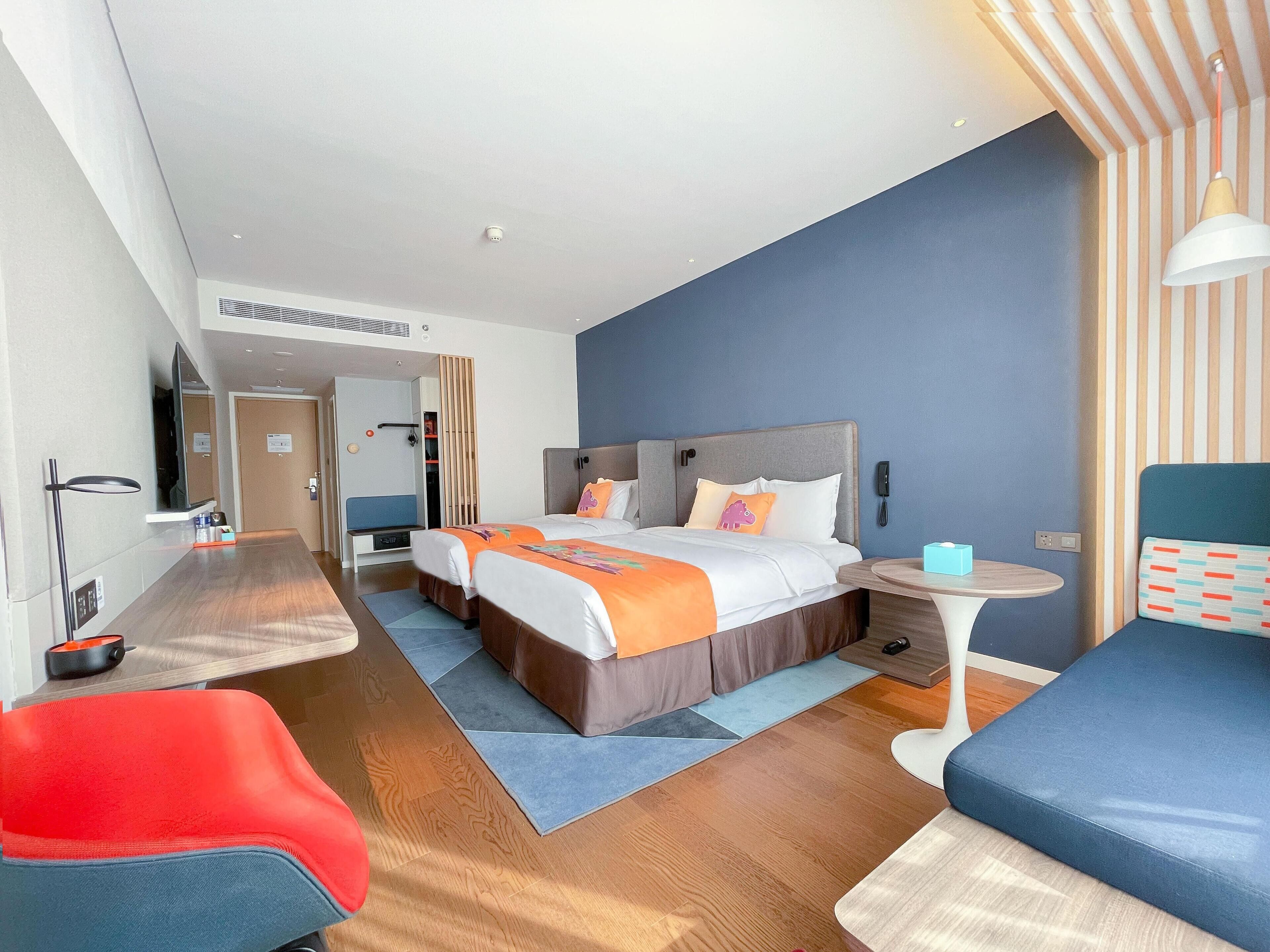 Quarto de hotel moderno com uma cama grande, uma escrivaninha, uma cadeira e uma pequena mesa.