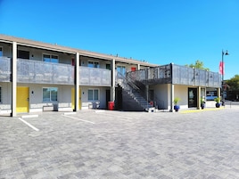 Um motel de dois andares com uma escadaria central, área externa coberta e estacionamento.