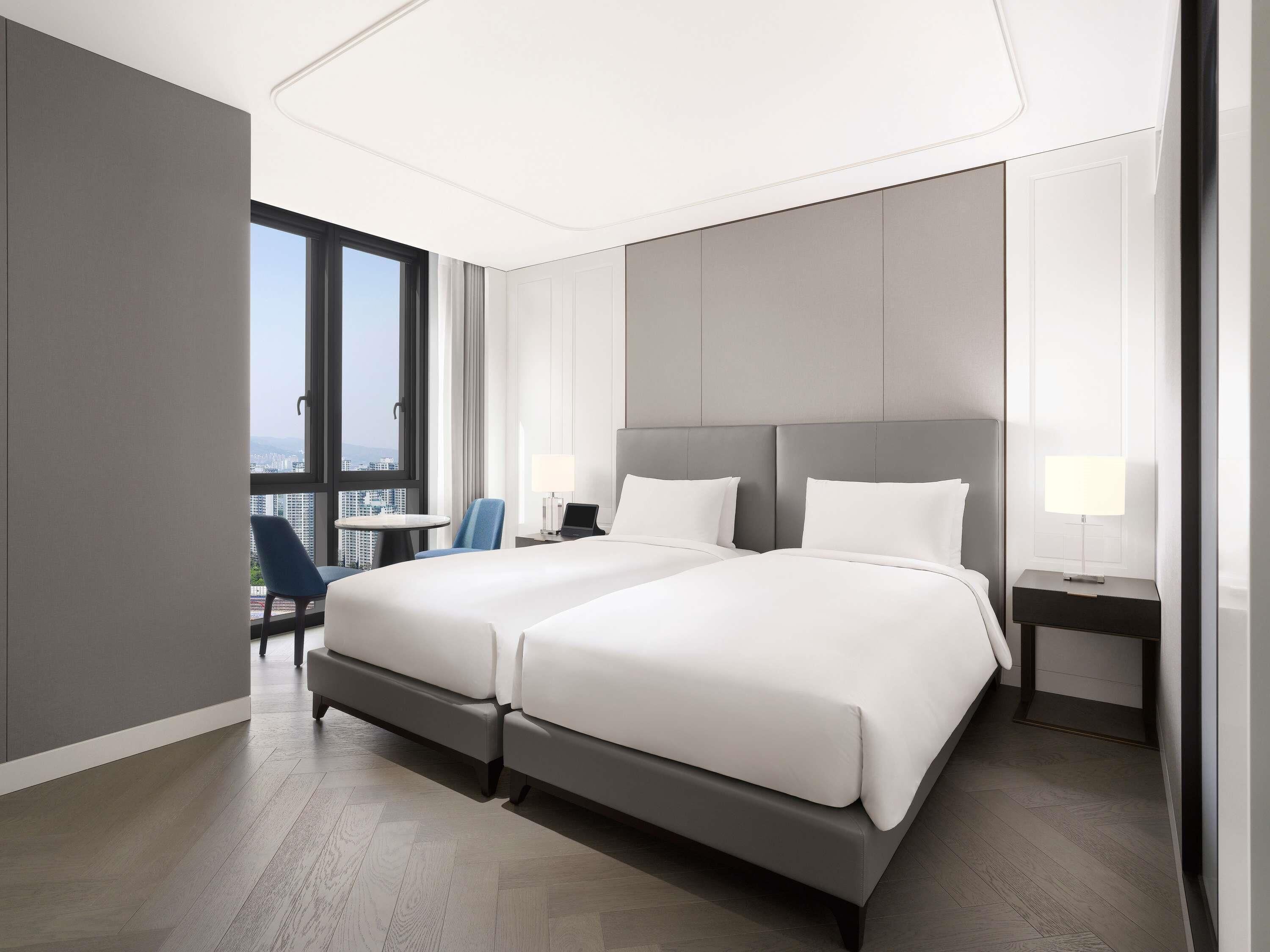 Quarto de hotel moderno com uma cama grande, uma escrivaninha, uma cadeira e vista para a cidade.