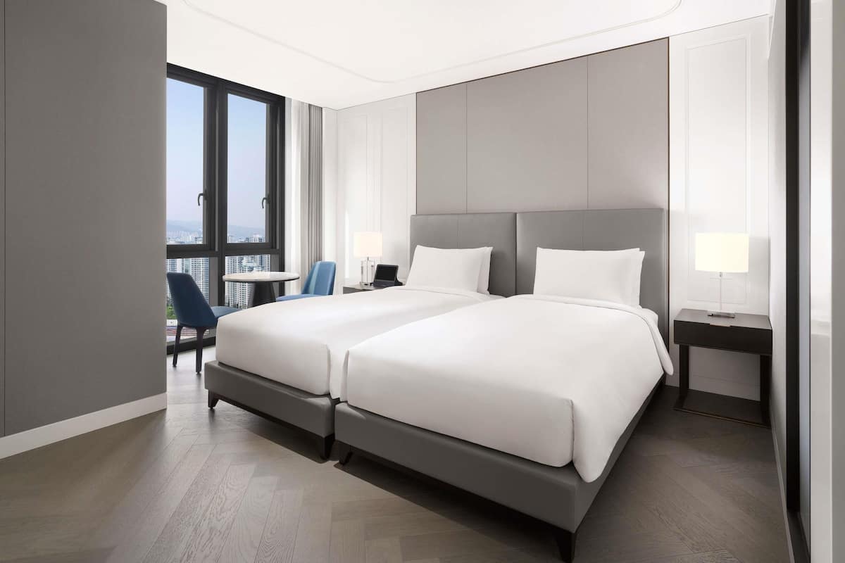 Quarto de hotel moderno com uma cama grande, uma escrivaninha, uma cadeira e vista para a cidade.