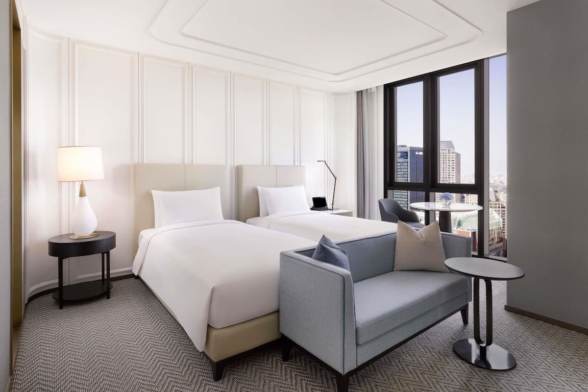 Quarto de hotel com duas camas, um sofá, uma pequena mesa e vista para a cidade.