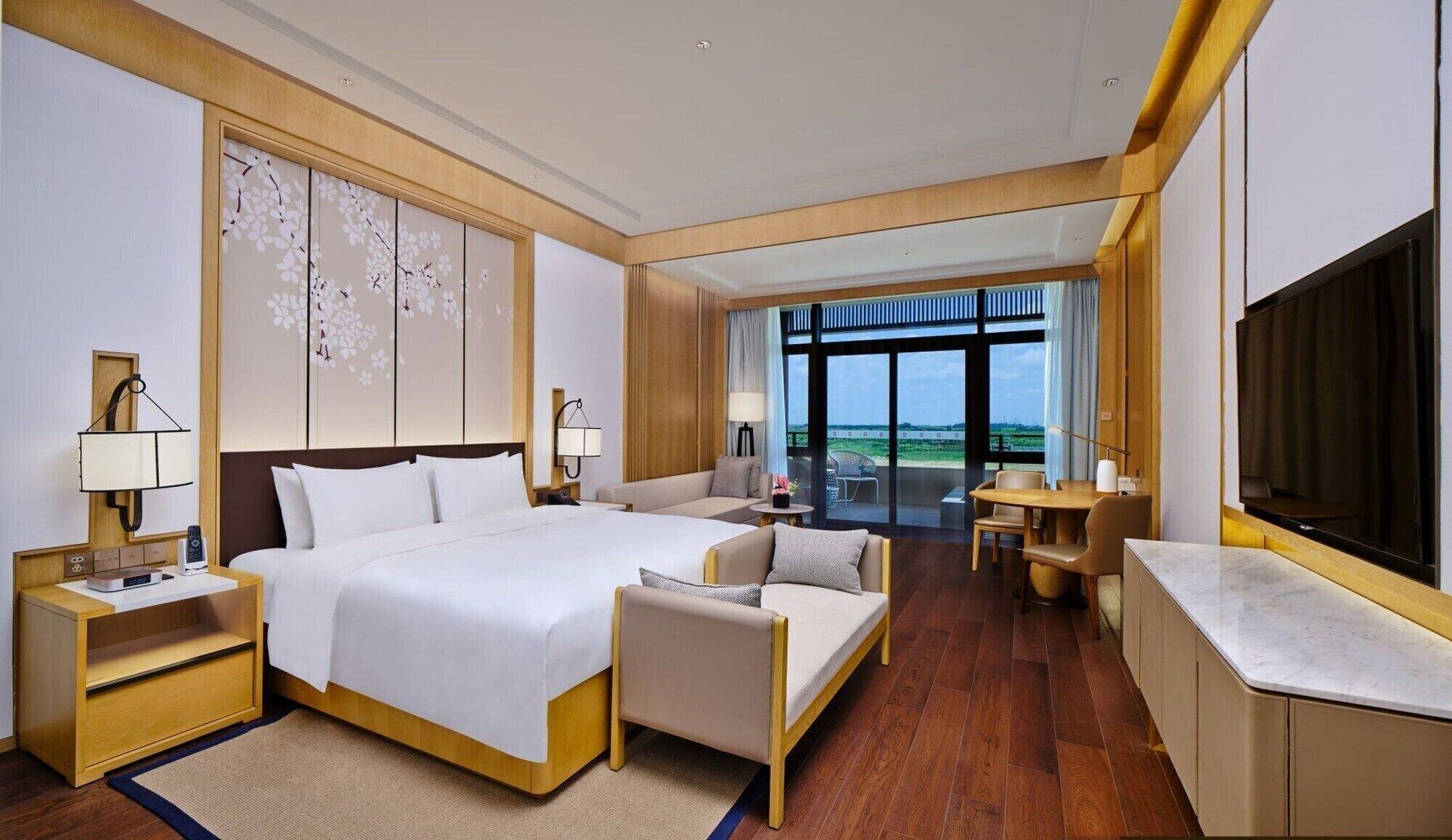 Quarto de hotel com cama grande, sofá, TV e vista para o exterior.