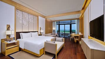 Quarto de hotel com cama grande, sofá, TV e vista para o exterior.