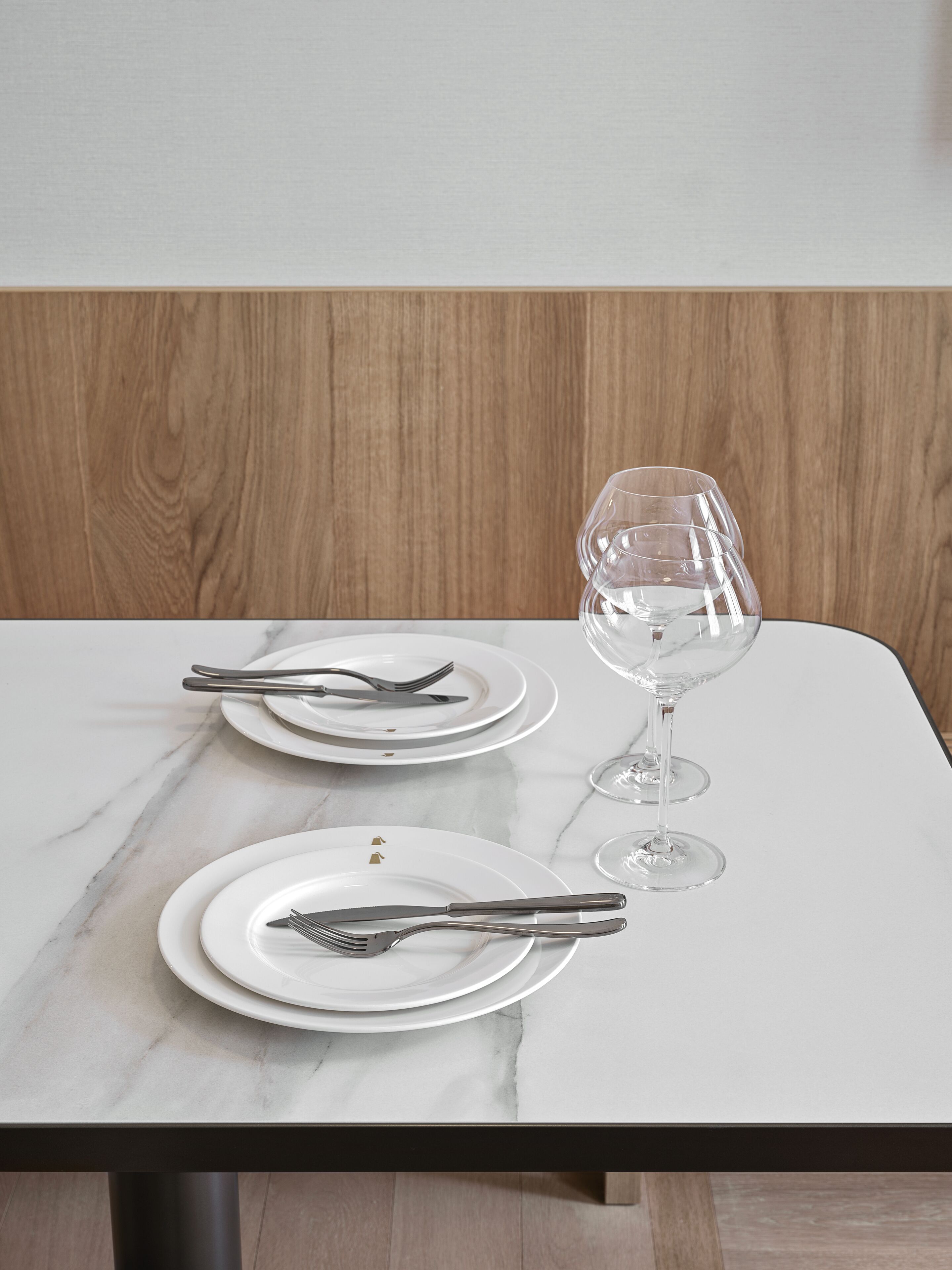 Mesa posta com pratos, talheres e uma taça de vinho sobre superfície de mármore.