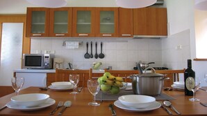 Cozinha com armários de madeira, micro-ondas, fogão e mesa de jantar posta com pratos, copos e utensílios.