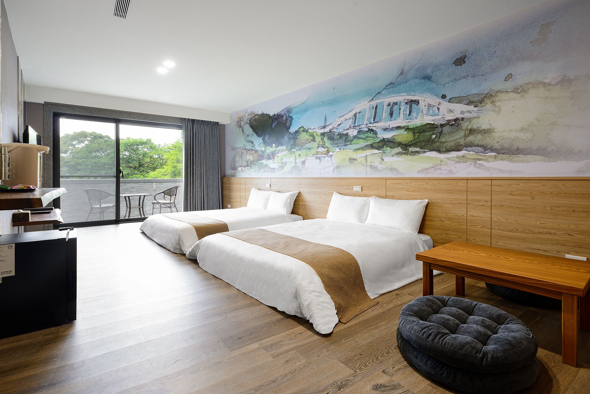 Quarto de hotel com duas camas, uma escrivaninha, uma cadeira, um banco e um quadro grande na parede.