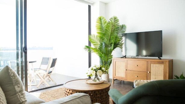 Uma sala de estar moderna com televisão de tela plana, um armário de madeira, uma mesa de centro redonda e uma grande planta em vaso.