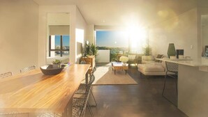 Sala moderna com mesa de jantar de madeira, sofá e mesa de centro. Vista para o exterior através de amplas janelas.
