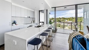 Uma cozinha moderna com uma ilha grande, banquetas e vista para a cidade através de janelas amplas.