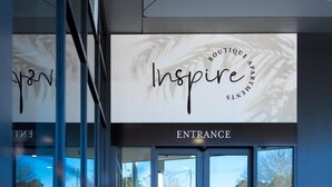 Um sinal com a inscrição 'Inspire Boutique Apartments', com uma placa de entrada abaixo.