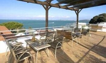 Terraço ao ar livre com mesas e cadeiras, com vista para um corpo de água e colinas.