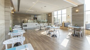 Um restaurante moderno com área de bar, piso de madeira e mobiliário branco.