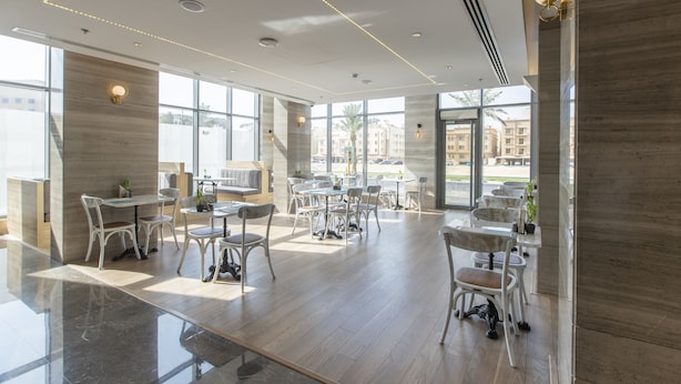 Um café moderno com piso de madeira, móveis brancos e grandes janelas com vista para a cidade.