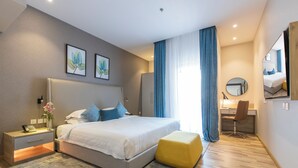 Quarto de hotel moderno com cama, mesa de cabeceira, escrivaninha, cadeira e um espelho grande.