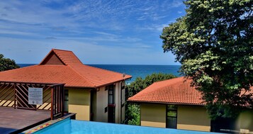 Um resort com piscina, vista para o mar e um edifício com telhado de telhas vermelhas.