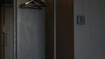 Quarto de hotel moderno com um banco de madeira, um cabideiro preto e um painel de controle na parede.