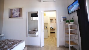 Quarto com cama, televisão, quadro e porta que dá para outro cômodo.