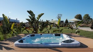 Uma banheira de hidromassagem em um deck de madeira, rodeada por plantas tropicais.