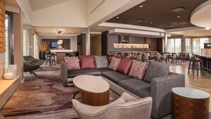 Um hall de hotel moderno com um amplo sofá de canto, área de bar e espaço para refeições.