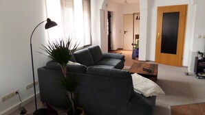 Uma sala de estar com um sofá cinzento, um abajur, uma planta em vaso e uma mesa de centro de madeira.
