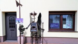 Escultura de metal de uma figura com uma placa indicando 'ELB-BUBUs' em frente a um edifício com porta e janela.