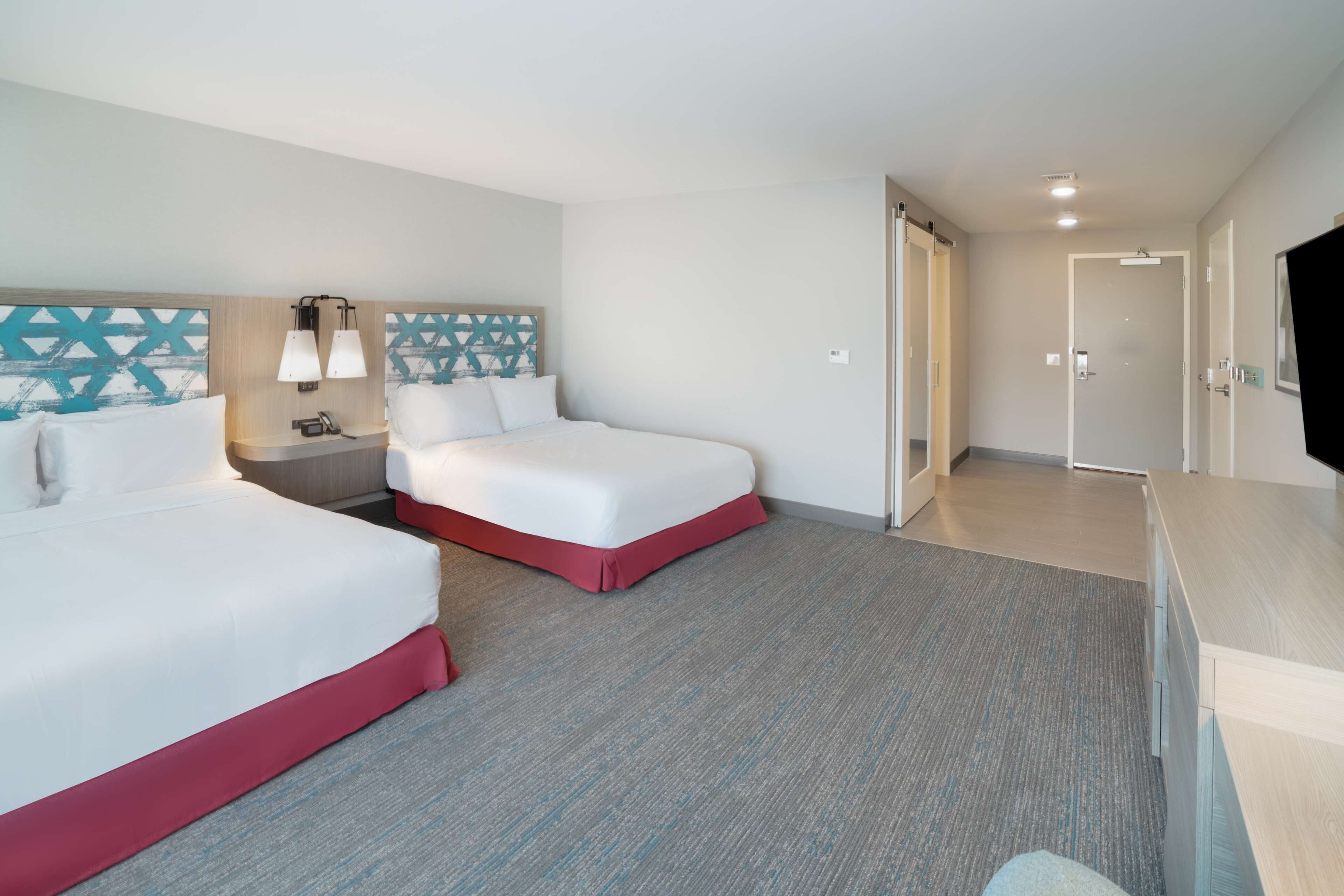 Quarto de hotel com duas camas, uma escrivaninha, televisão e porta de banheiro.