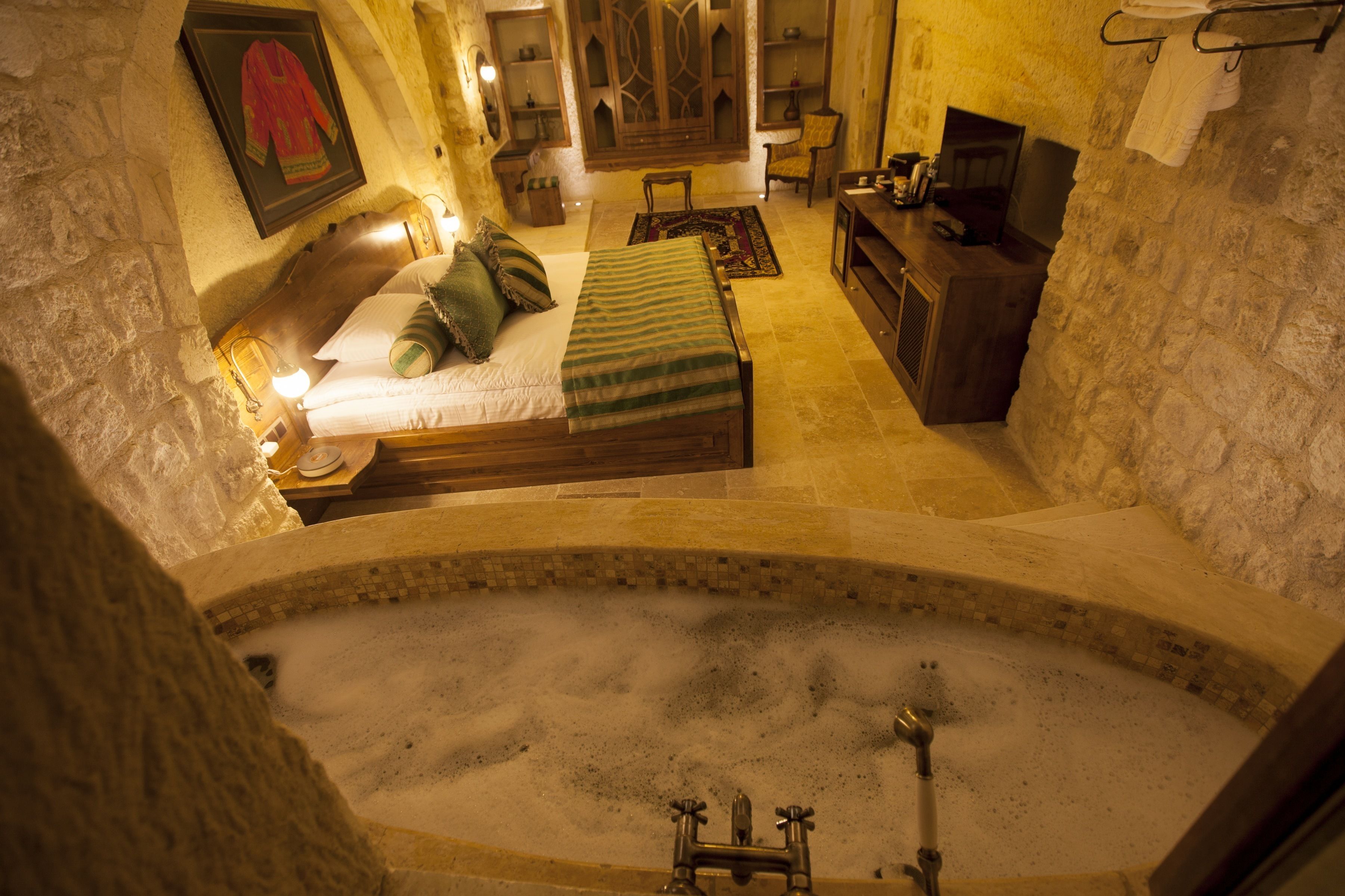 Quarto com parede de pedra, cama com almofadas, cómoda de madeira, cadeira e banheira com espuma.