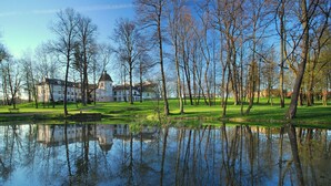 Um edifício grande refletido em águas calmas, rodeado por árvores e um espaço gramado.