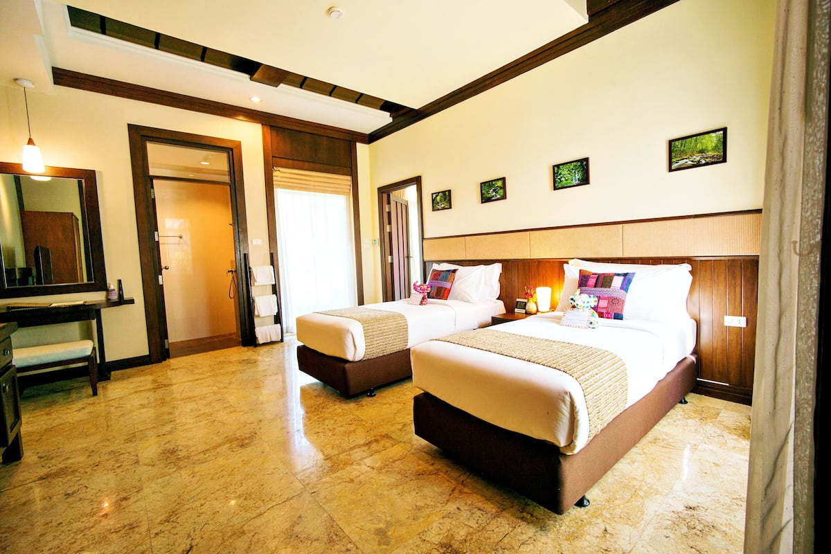Quarto de hotel com duas camas, cabeceira de madeira, espelho grande e piso de mármore.