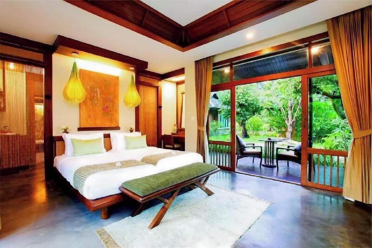 Quarto espaçoso com uma cama grande, um banco de madeira e vista para um verde exuberante pelas janelas amplas.