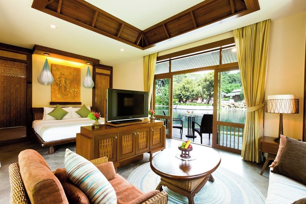 Quarto de hotel com cama, televisão, sofá, mesa de centro e vista para o exterior.