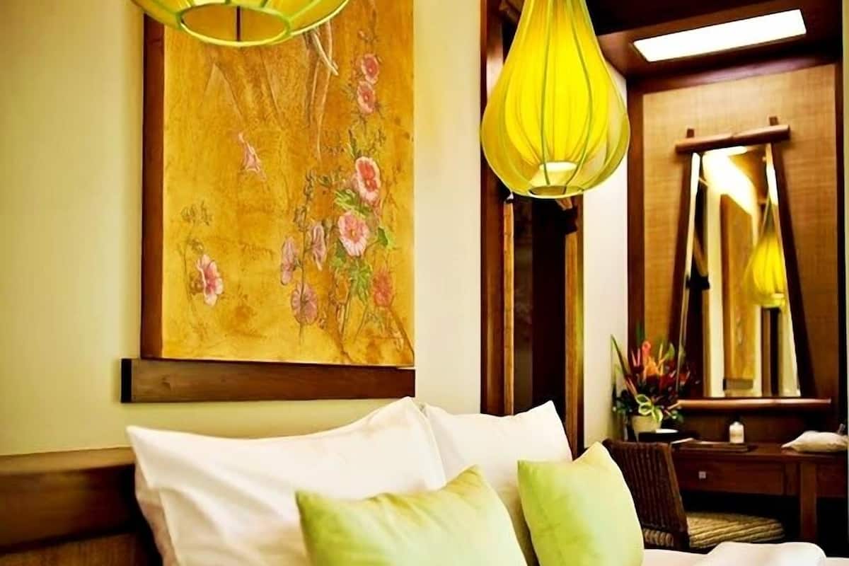 Quarto de hotel com uma cama grande, duas almofadas verdes e duas luminárias pendentes.