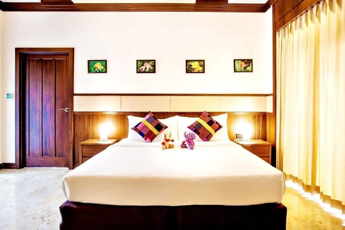 Quarto de hotel com uma cama grande, duas mesas de cabeceira e cabeceira de madeira. Há quatro quadros na parede acima da cama.