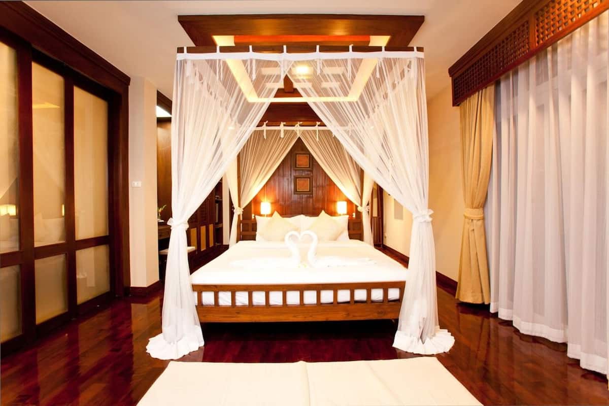 Um quarto espaçoso com uma cama grande, dossel branco, cabeceira de madeira e um tapete vermelho.