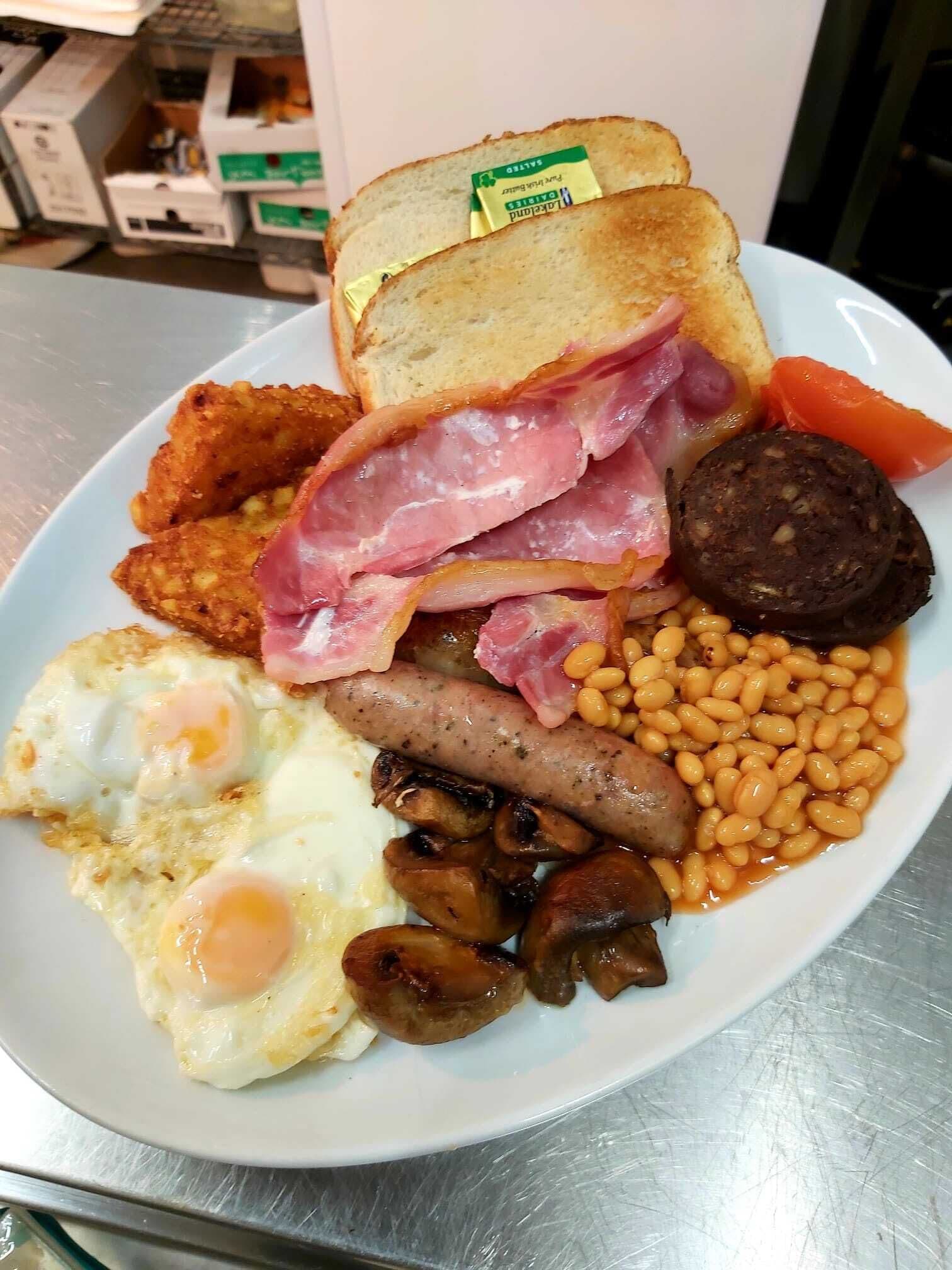 Um prato de comida de café da manhã com ovos, salsichas, feijão, torradas e bacon.