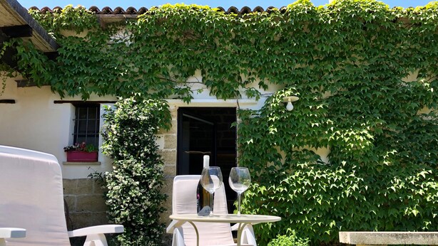 Um pátio com móveis de jardim brancos, uma mesa com duas taças de vinho e um banco.