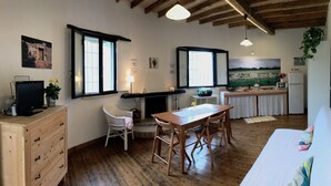 Um quarto aconchegante com uma mesa de jantar de madeira, cadeiras brancas, uma televisão e uma cama com roupa de cama colorida.