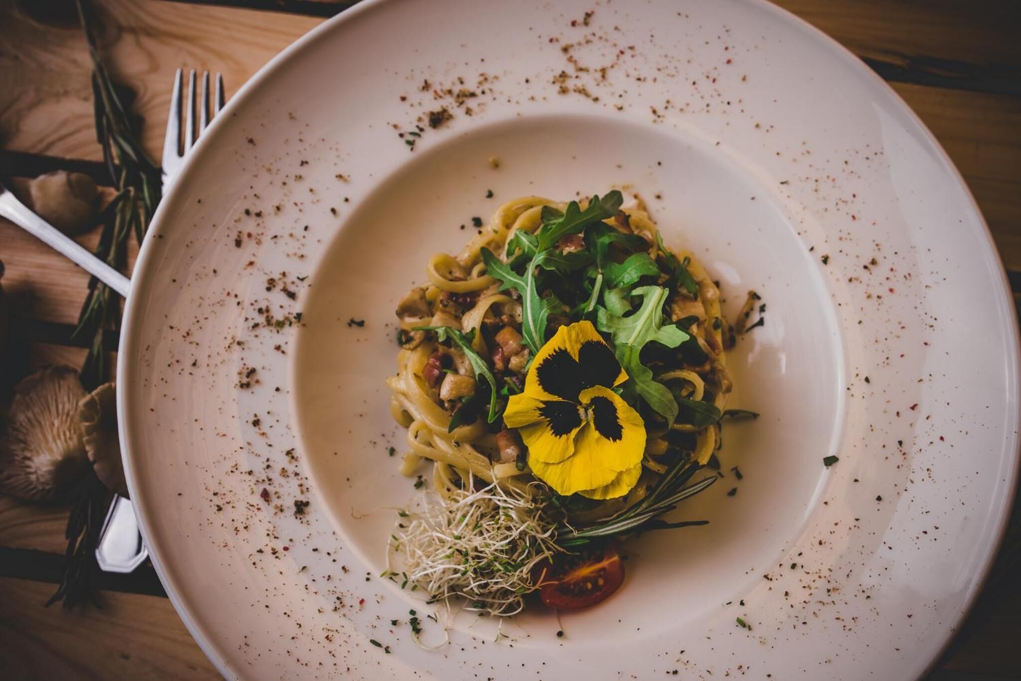 Um prato de massa com vegetais e um enfeite de flor amarela.