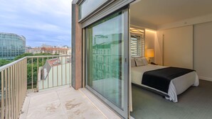 Quarto de hotel com varanda, uma cama, mesa de cabeceira e janela com vista para a cidade.