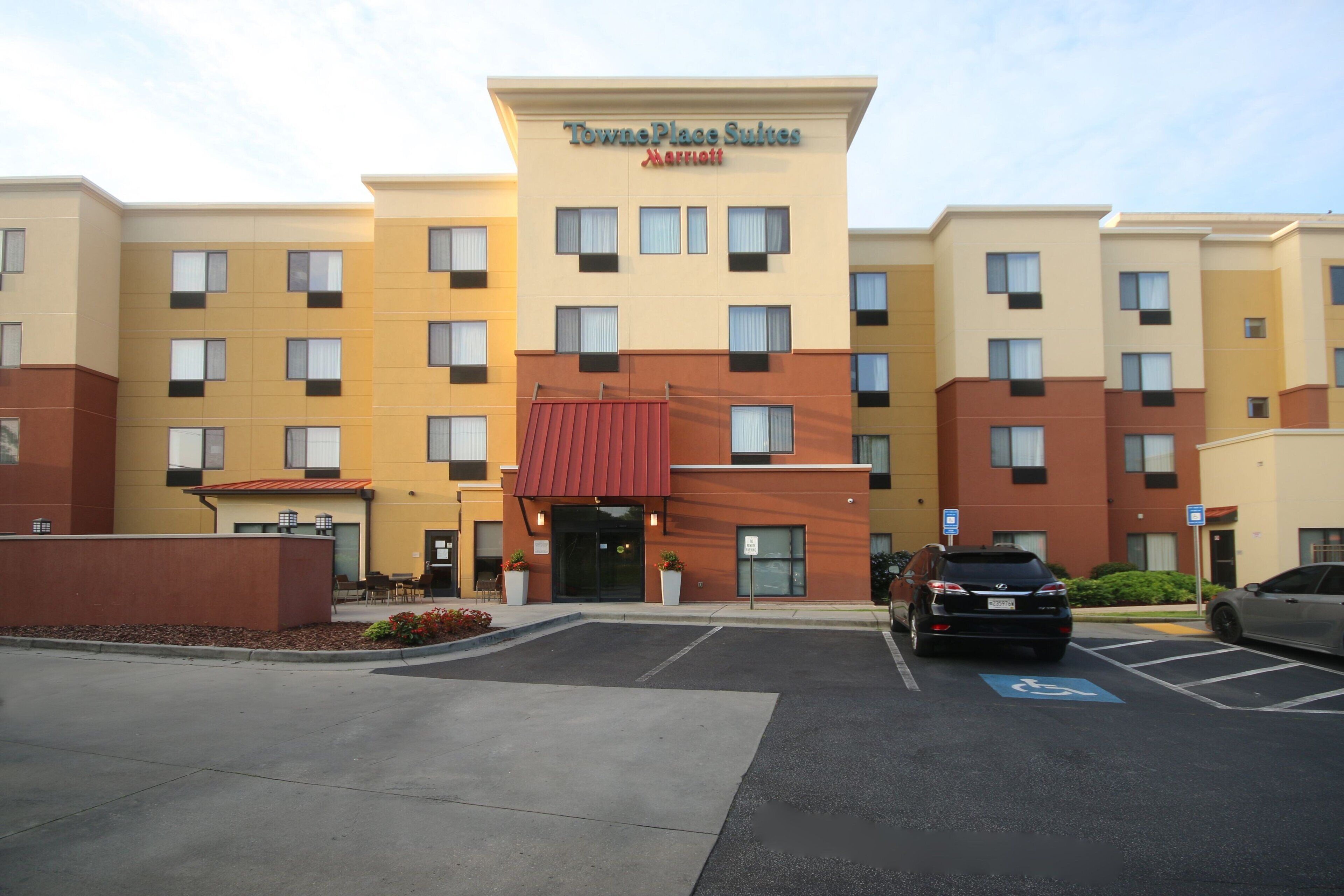 Um hotel com vários andares, entrada central, estacionamento e uma placa com a inscrição 'TownePlace Suites Marriott'.