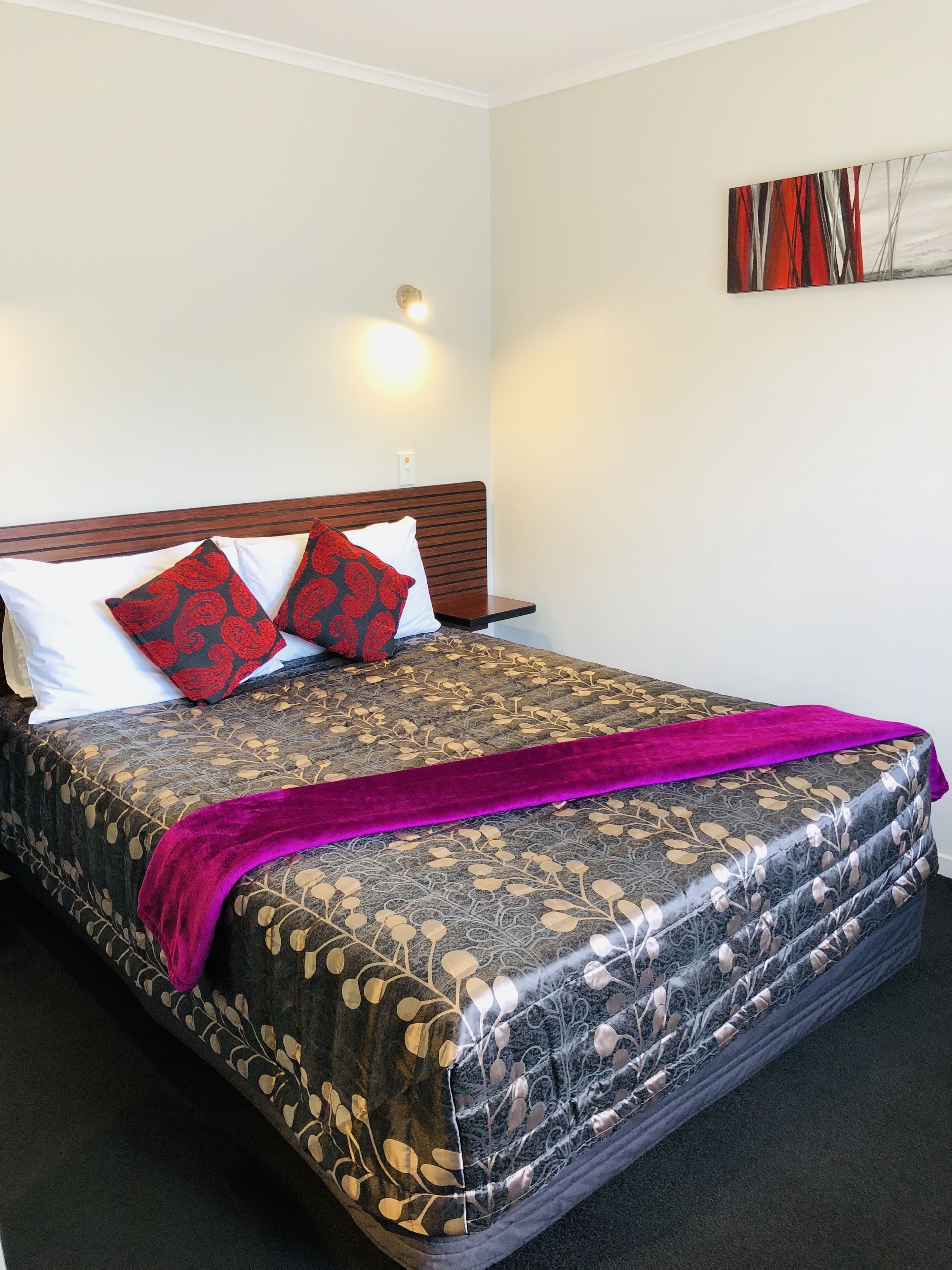 Cama bem arrumada com roupa de cama estampada, cabeceira e luminária fixada na parede.