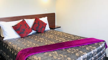 Cama bem arrumada com roupa de cama estampada, cabeceira e luminária fixada na parede.