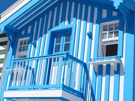 Um edifício com fachada azul e branca listrada, uma varanda com guarda-corpo e várias janelas.