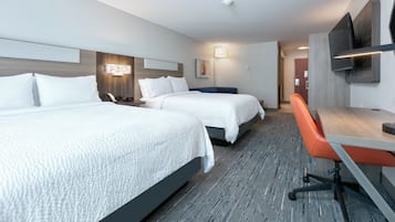 Quarto de hotel com duas camas, uma mesa, uma cadeira, televisão de tela plana e luminária na parede.
