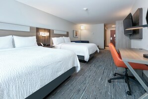 Quarto de hotel com duas camas, uma mesa, uma cadeira, televisão de tela plana e luminária na parede.