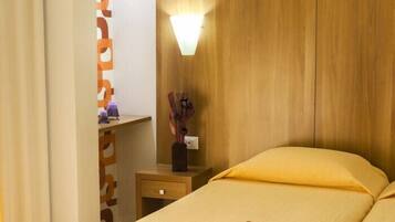Quarto de hotel com guarda-roupa de madeira, mesa de cabeceira com um vaso de flores secas e uma cama com colcha amarela.